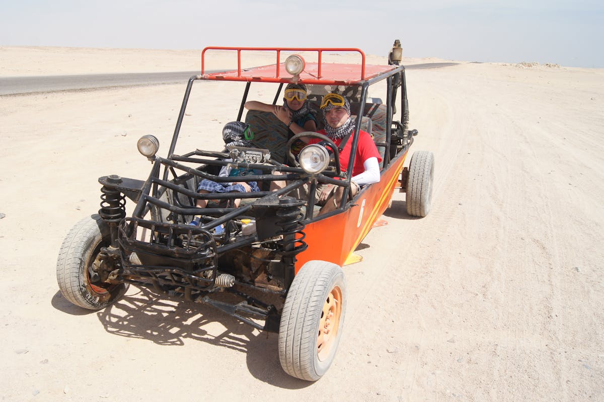 Two open-top buggies driving through desert terrain under bright sun