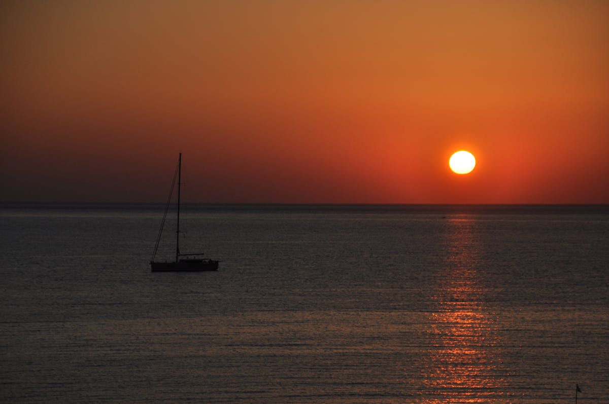 A sailboat silhouetted against a vibrant sunset over calm Mediterranean waters
