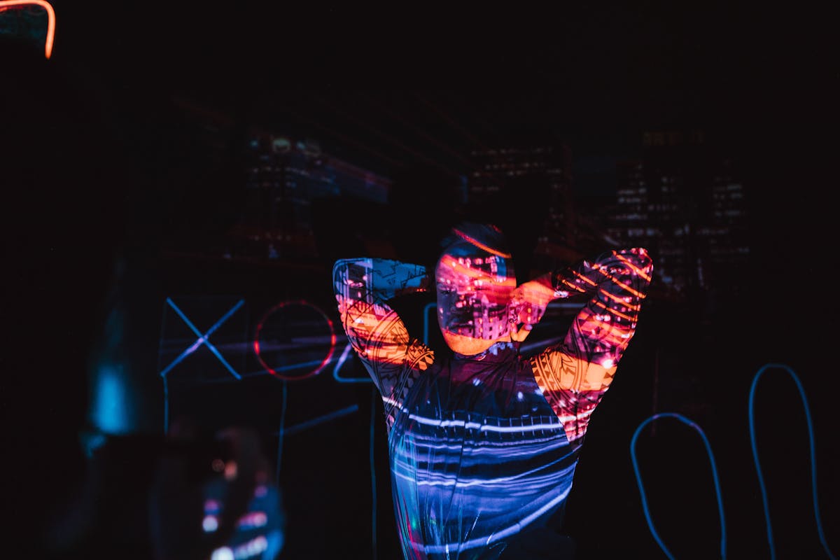 A person standing in a dark room illuminated by colorful neon projections
