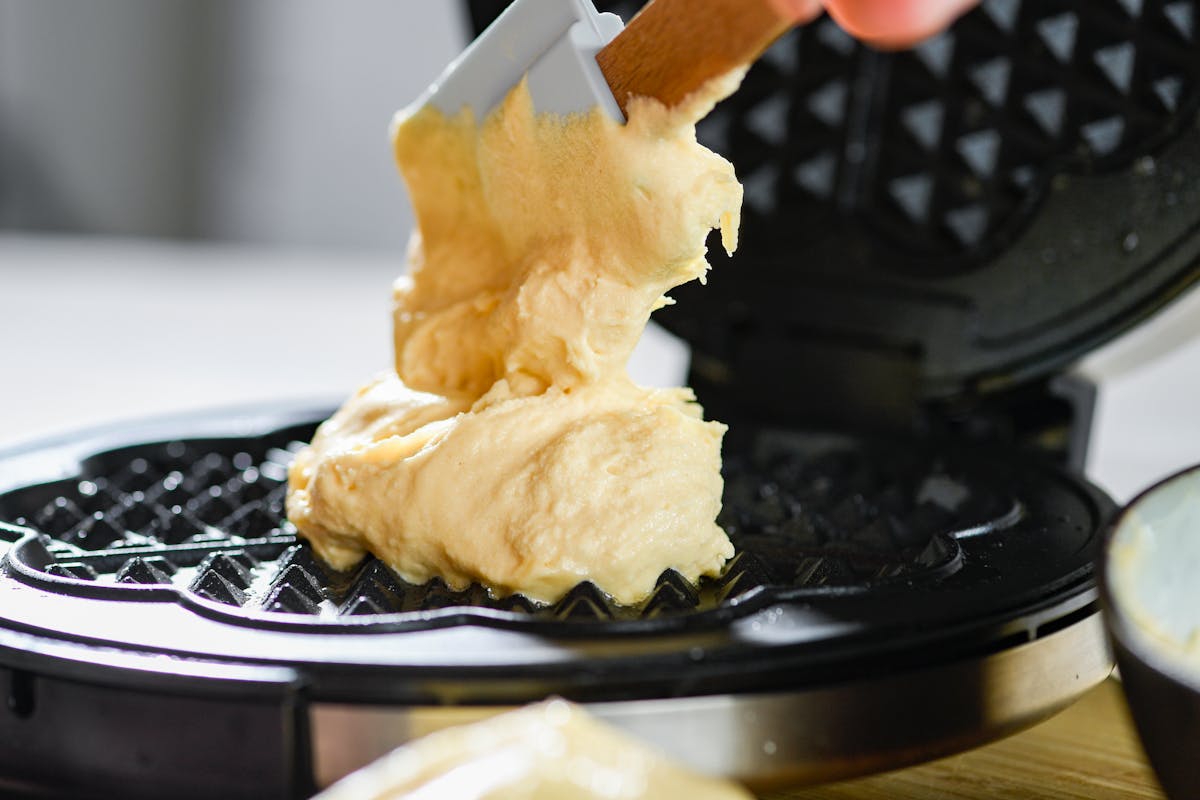 Raw waffle dough being spread on a hot waffle maker
