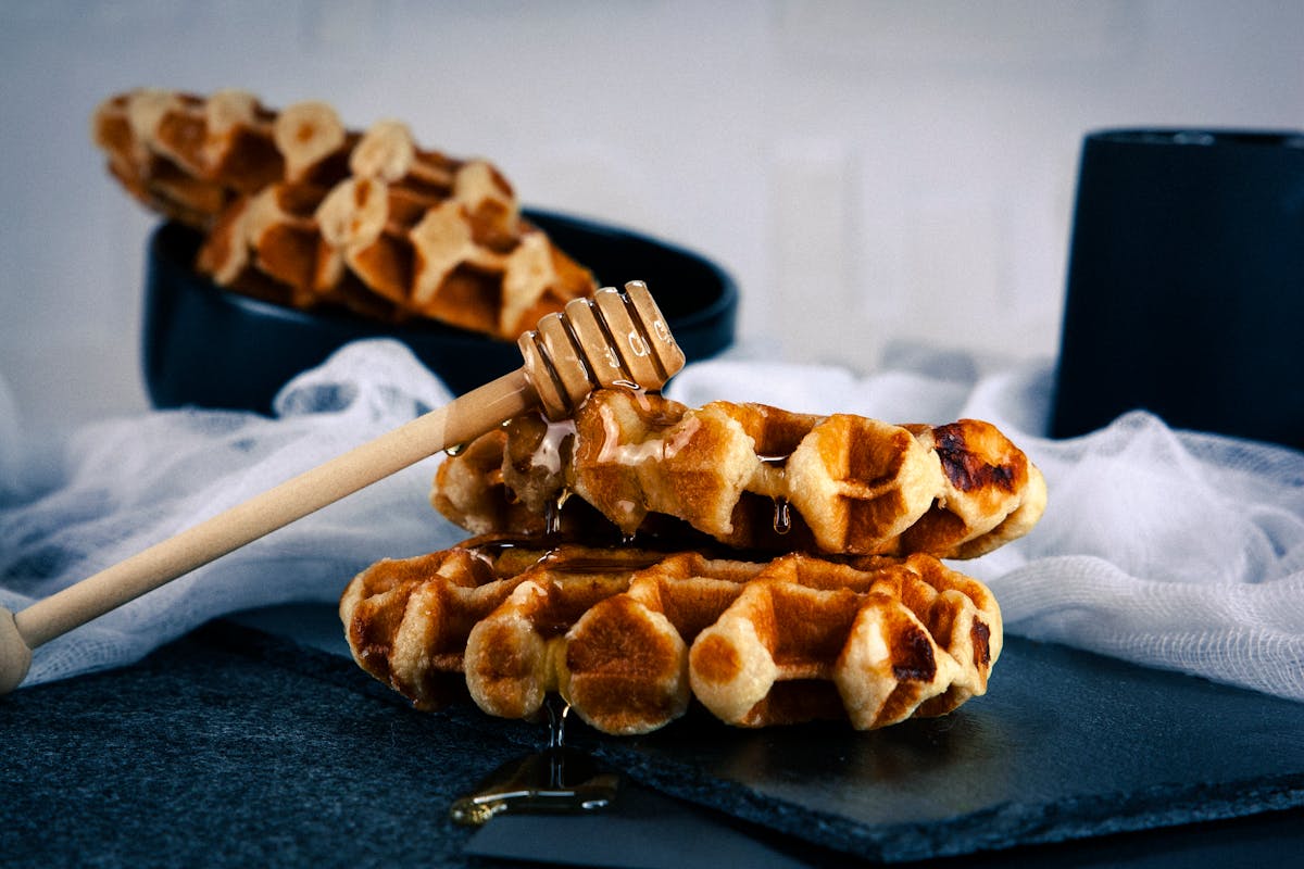 Golden Belgian waffles drizzled with honey on a black plate