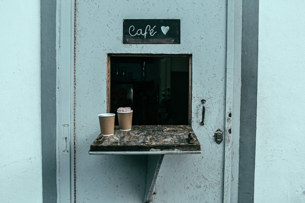 A quaint cafe window with two coffee cups on a rustic shelf