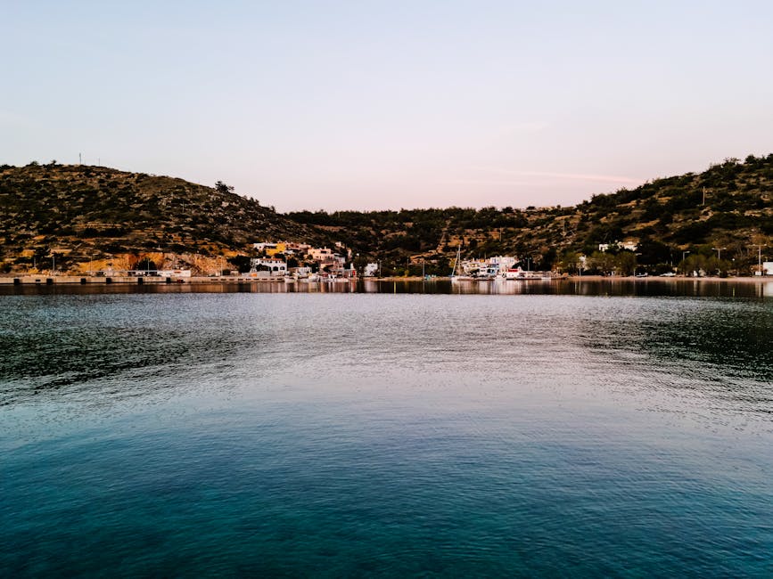 Tranquil Greek waterfront with hills and calm water under a soft sunset sky