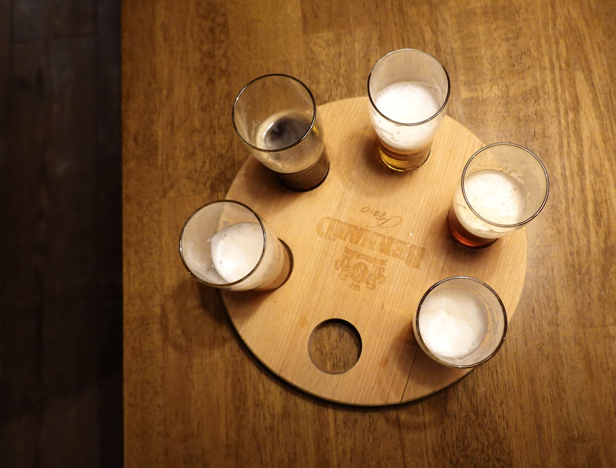 Overhead shot of five beer glasses with foam on a round wooden tray