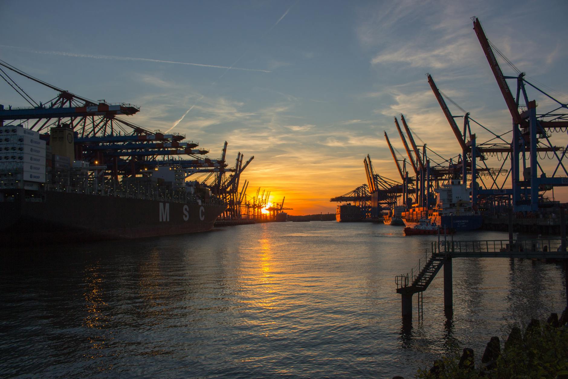 Ships at Hamburg port during sunset with industrial cranes in background