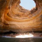 Interior of Benagil sea cave with sunlight illuminating sandy beach through dome opening