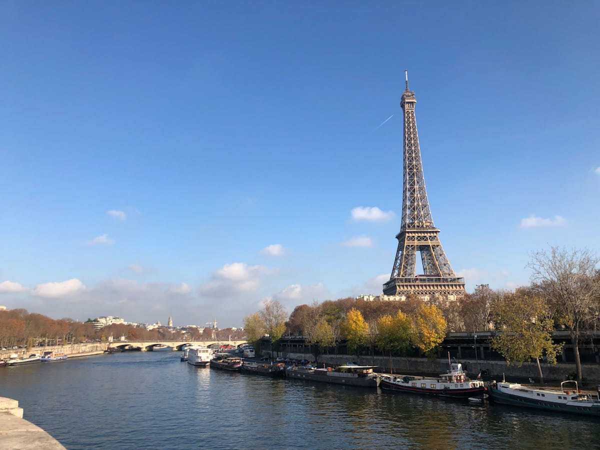 Eiffel Tower near the Seine River with boats floating under a clear blue sky