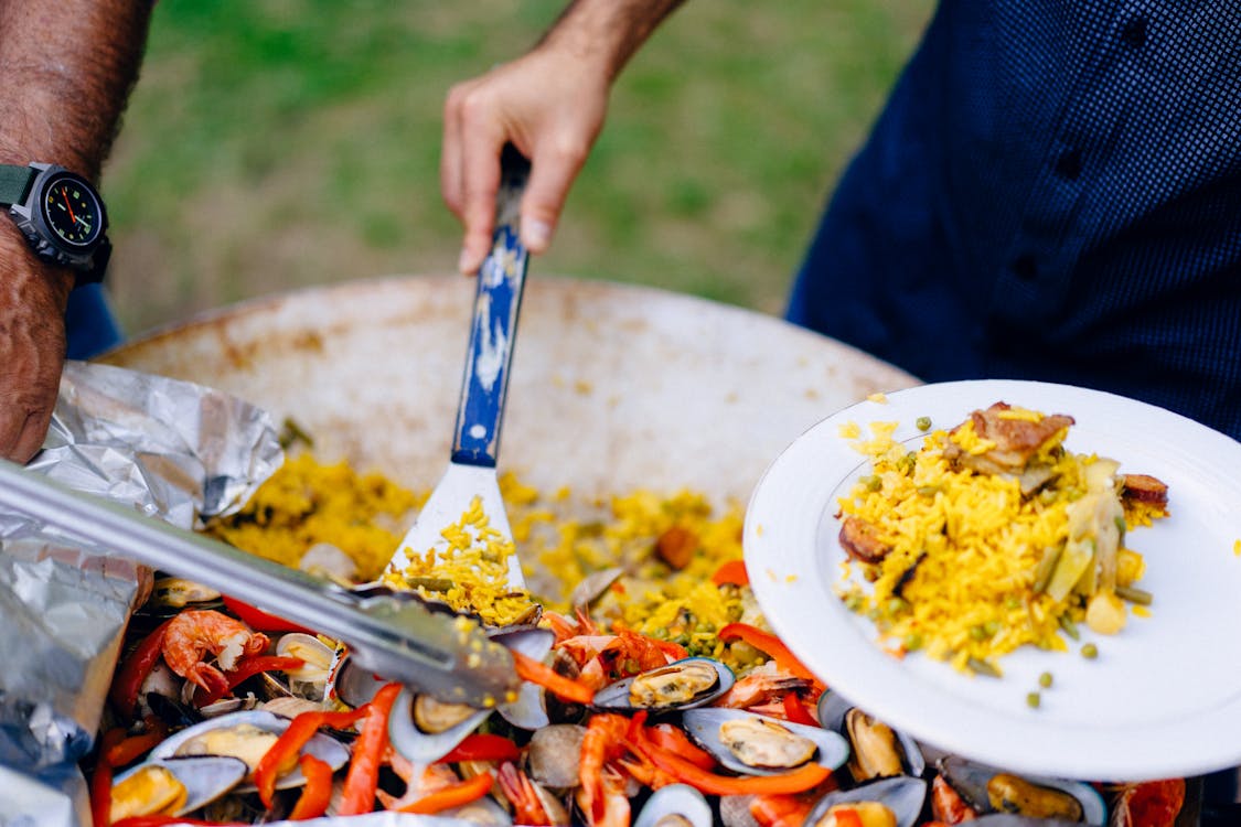 Hands serving Spanish paella with shrimp and mussels
