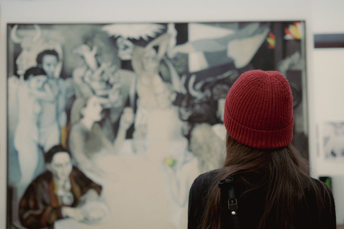 A woman in a red knit hat observes a painting in an art gallery