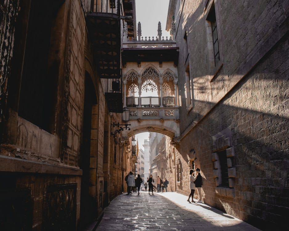 People walking under the ornate Pont del Bisbe bridge in Barcelona Gothic Quarter