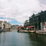 Tour boats cruising along a tree-lined Amsterdam canal with traditional Dutch buildings