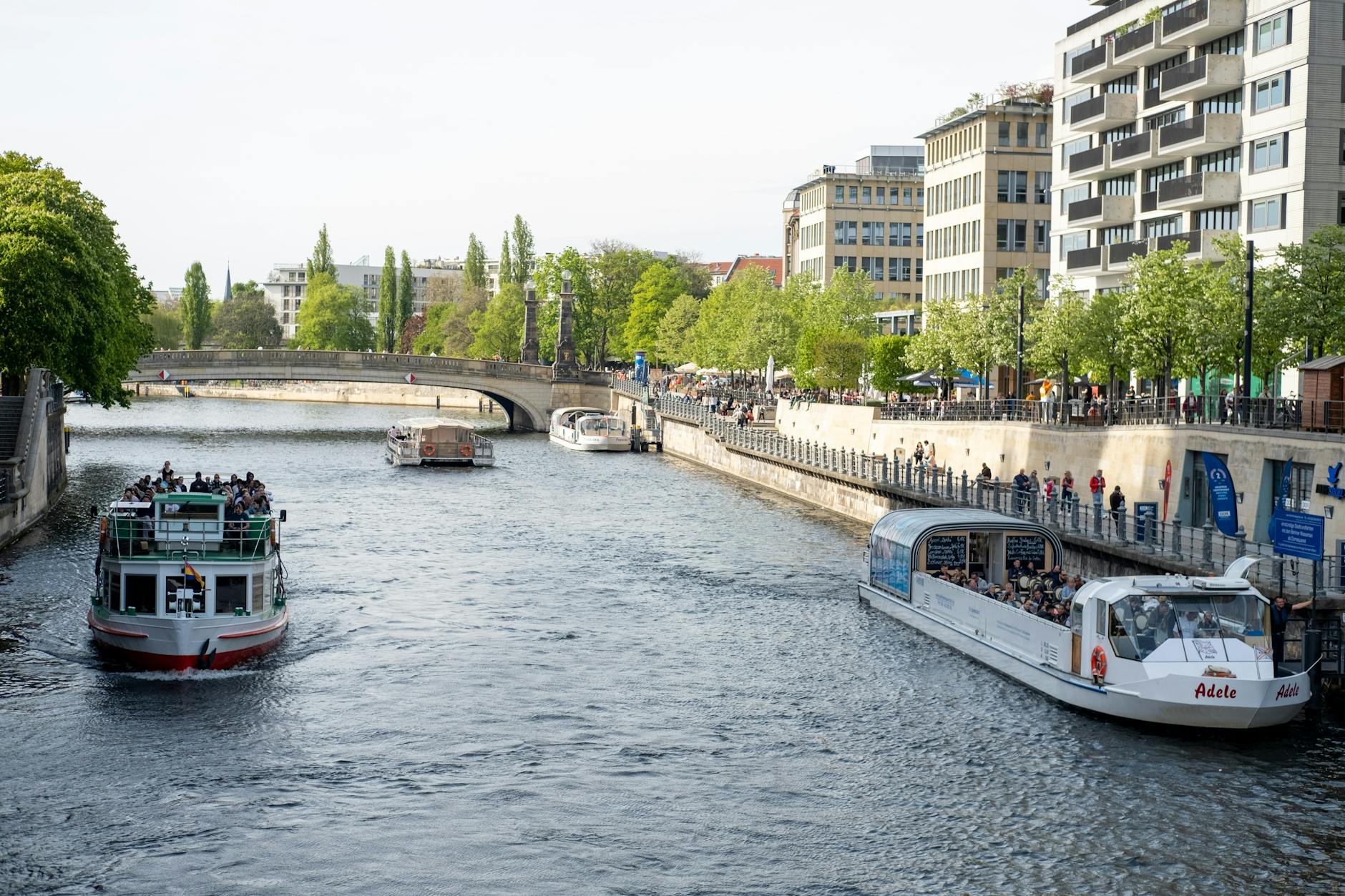 Boats cruising along a Berlin river with lush greenery and urban skyline