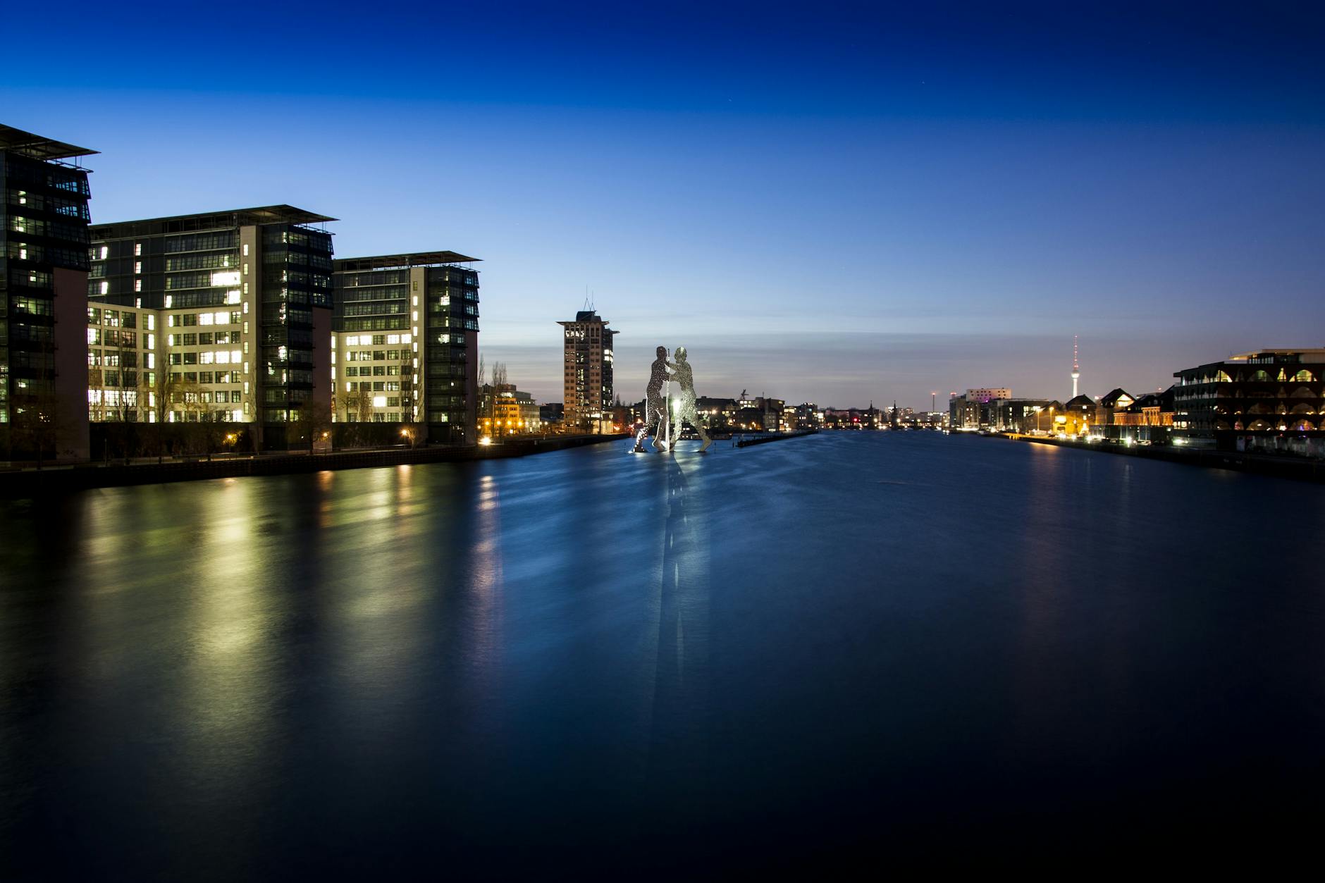 Berlin skyline at night featuring the Molecule Man sculpture along the river