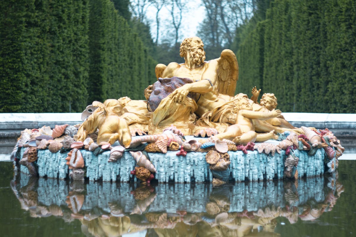 Golden statues at the Saturn Fountain reflecting in water at Versailles gardens