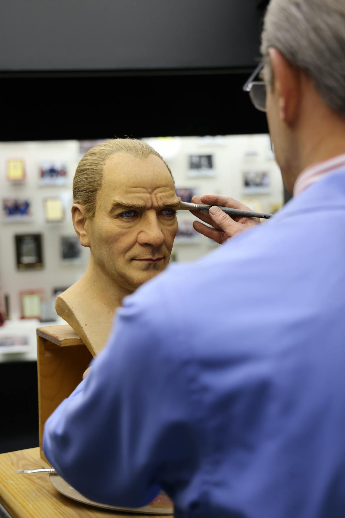 An artist meticulously paints a lifelike wax bust in a studio setting