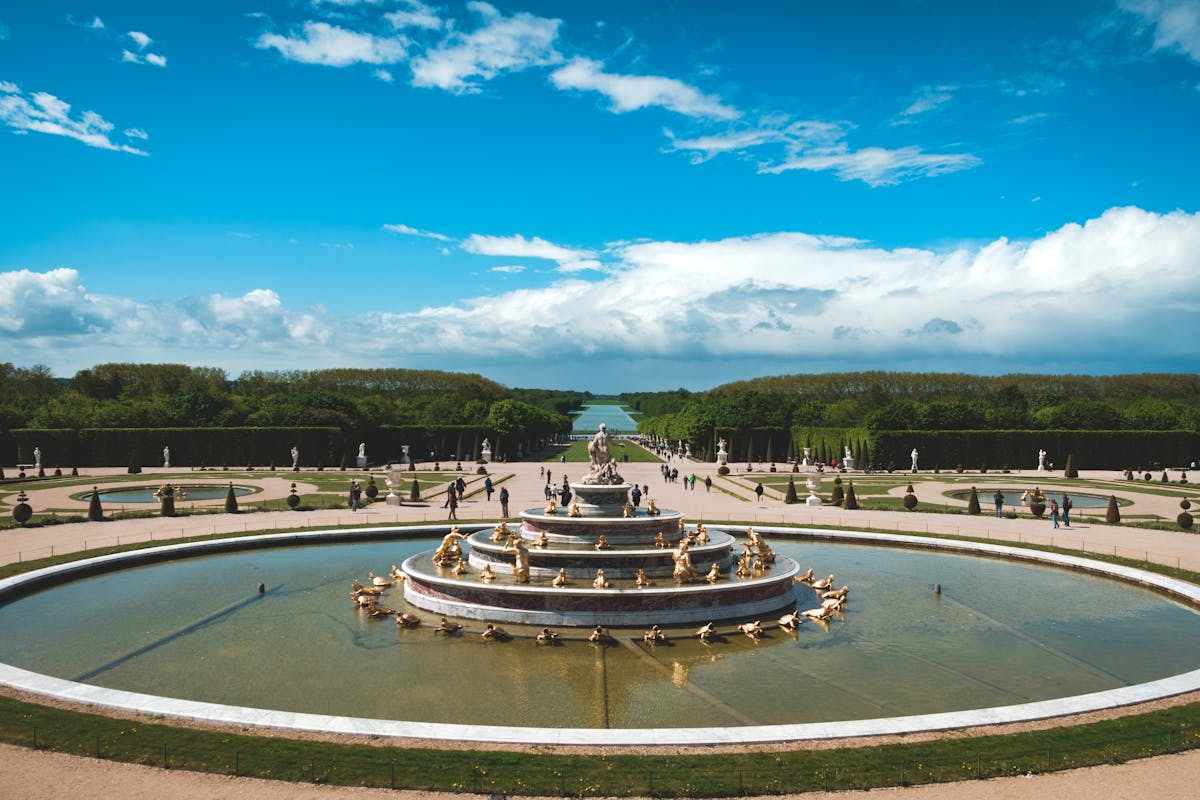 Sunlit fountain in the formal gardens of Versailles with blue sky