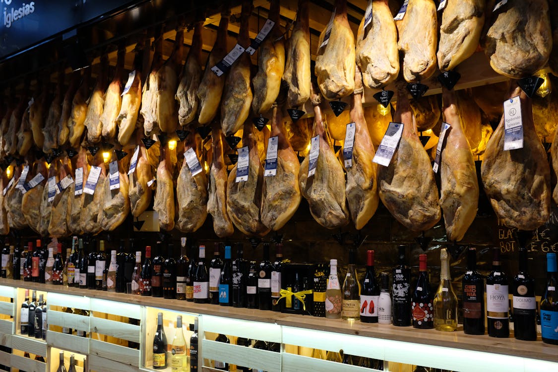 A display of hanging Spanish jamon with wine bottles in a Barcelona market