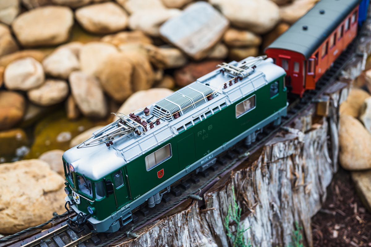 Green model train navigating a garden track with natural rocks