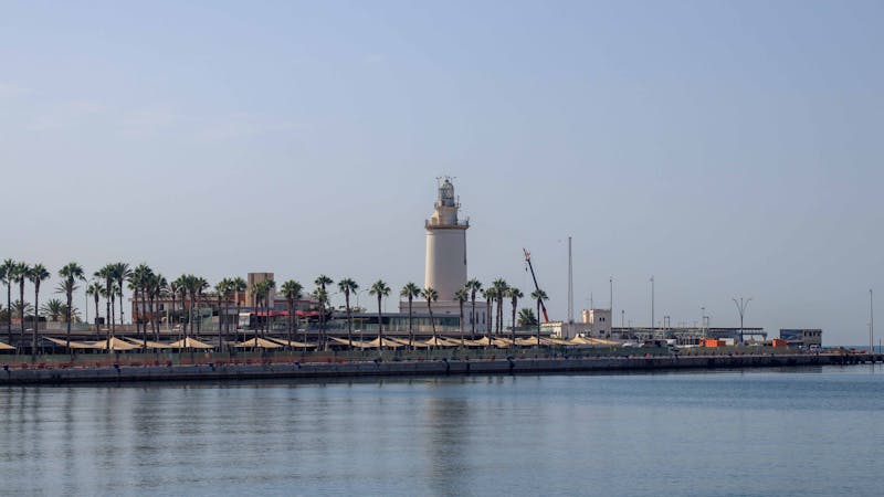 White lighthouse on the Malaga coastline surrounded by palm trees under blue sky
