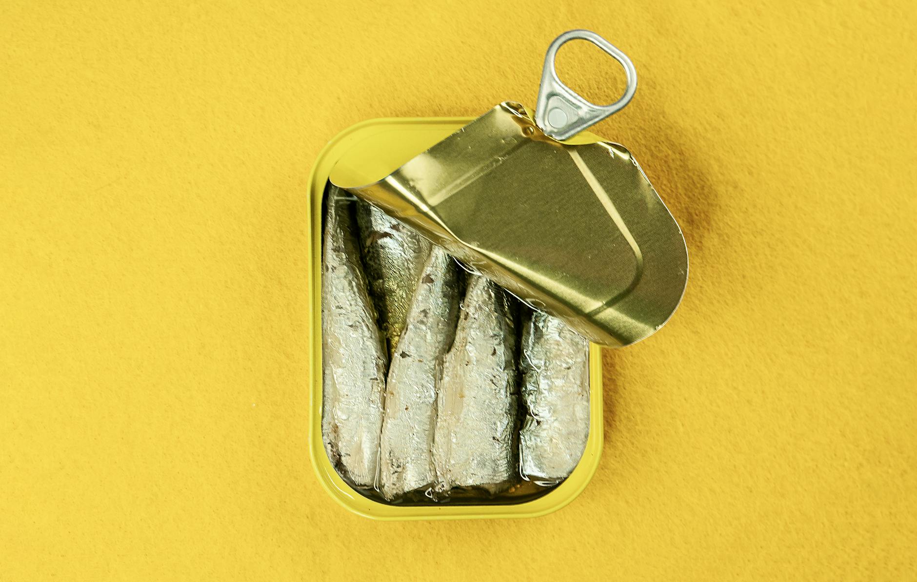 Opened tin of Portuguese sardines on a bright yellow background