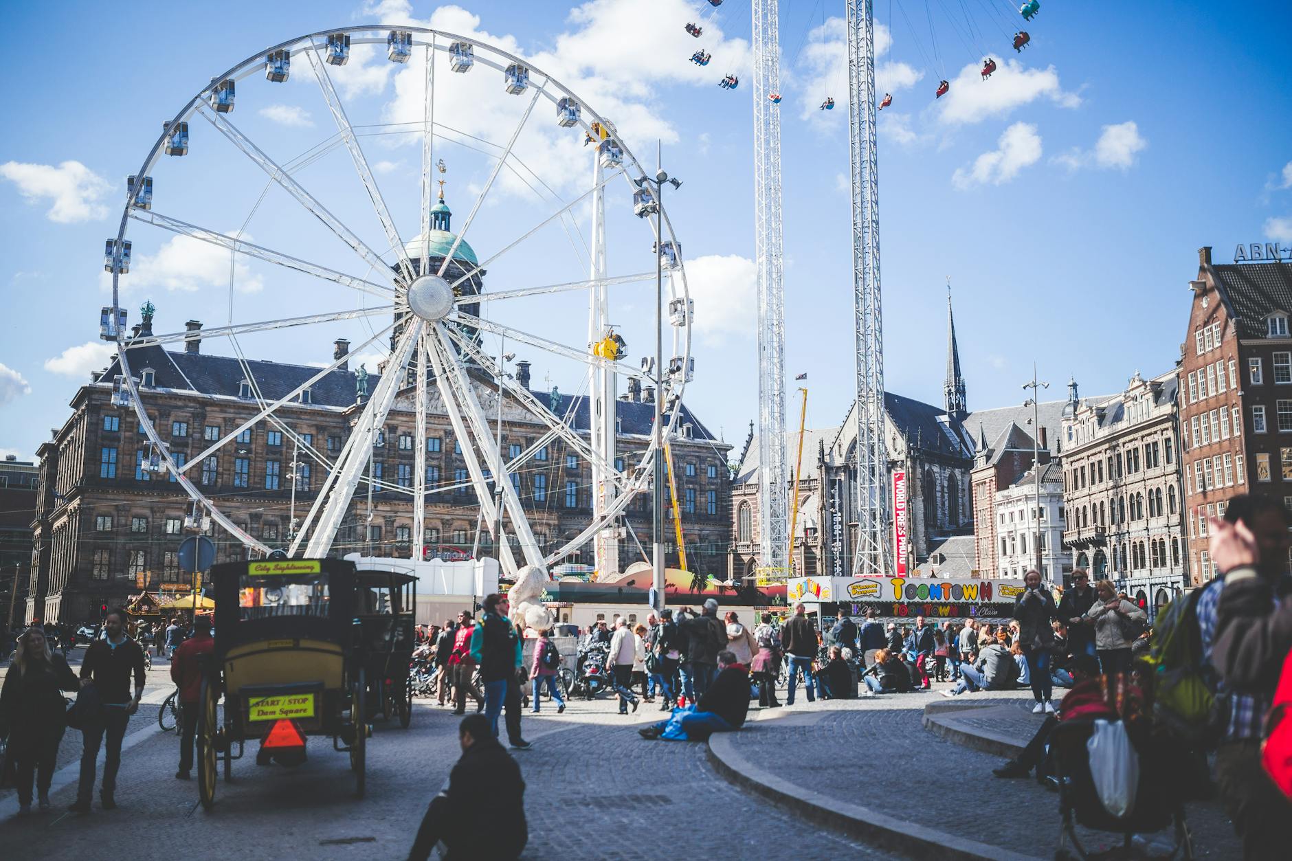 People enjoying a lively day at a colorful city attraction with a Ferris wheel under a blue sky