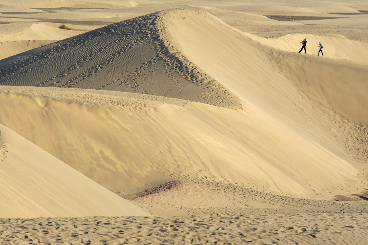 Two people walking across the sand dunes of Maspalomas under a blue sky