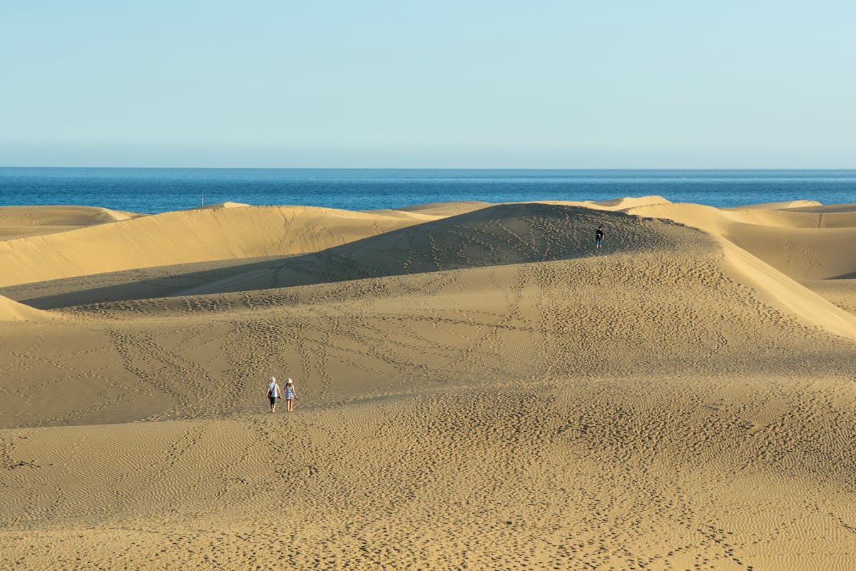 A couple walks across sandy Maspalomas dunes with the sea in the background
