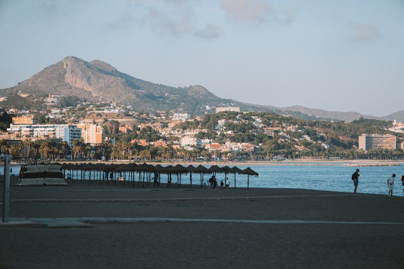 Sandy beach in Malaga with sunbathers, blue Mediterranean water, and mountain backdrop