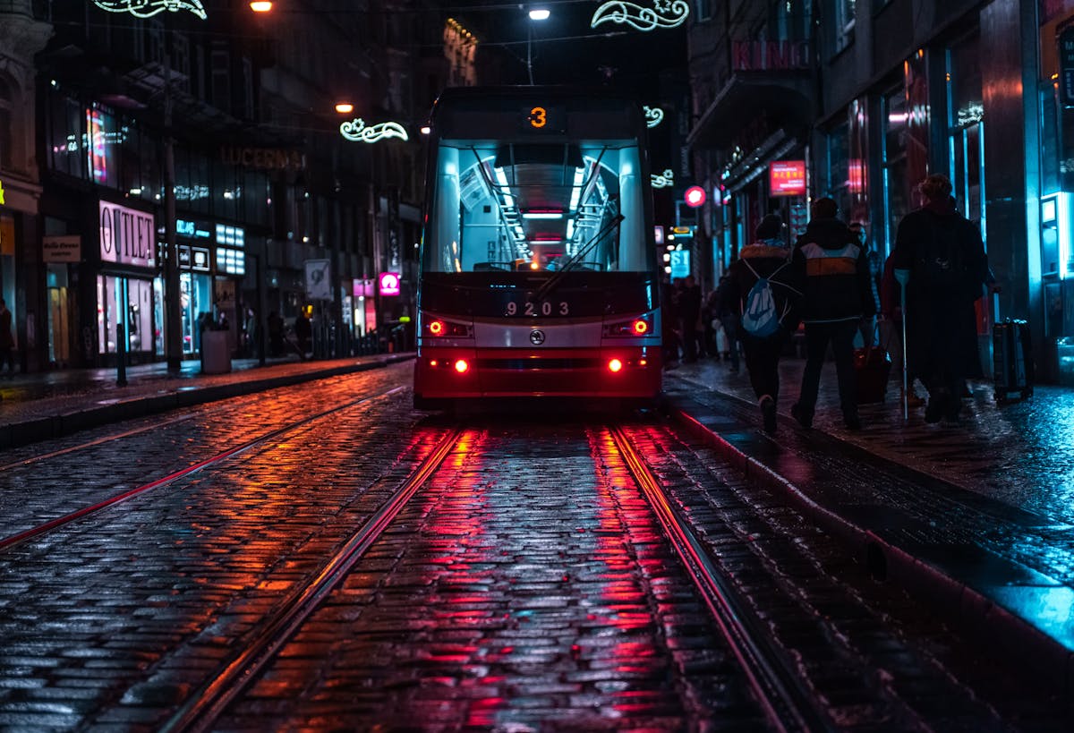 Prague tram running down a wet cobblestone street reflecting city lights on a rainy evening