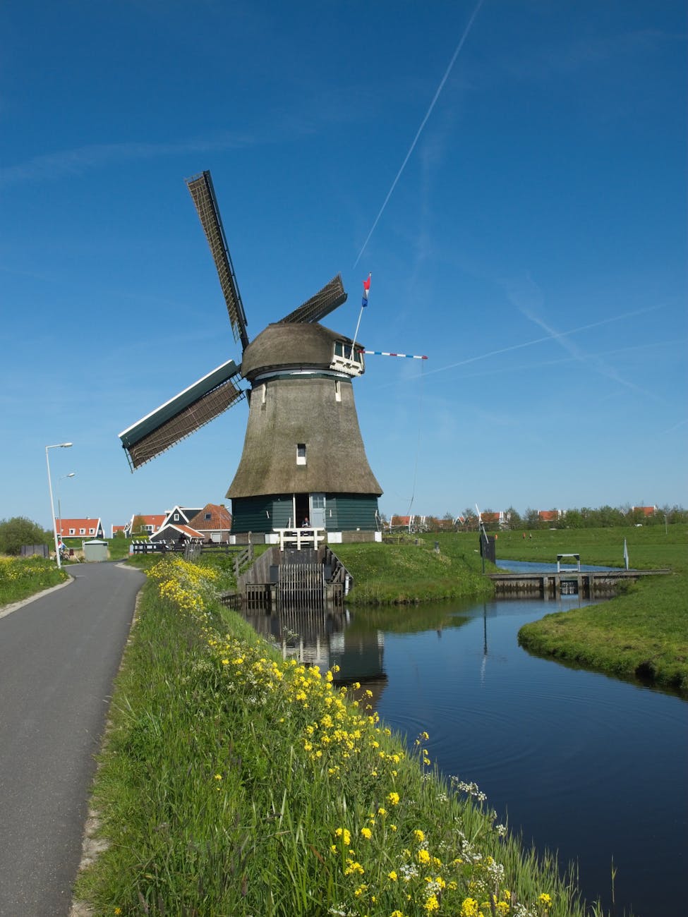 Traditional Dutch windmill by a river in a rural village under a clear blue sky