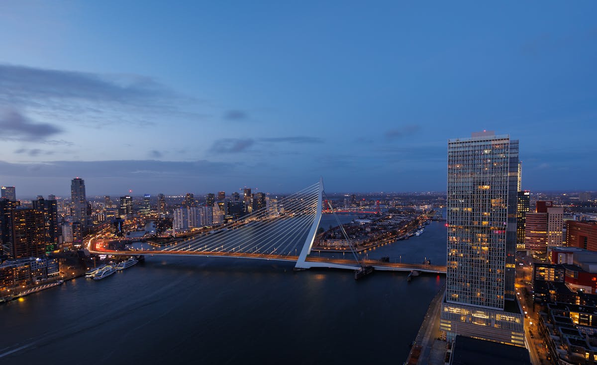 The Erasmus Bridge lit up at dusk with Rotterdam skyline reflected in the Maas River