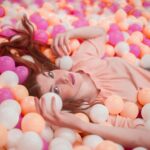 A woman lying in a vibrant ball pit filled with colorful balls at an interactive experience