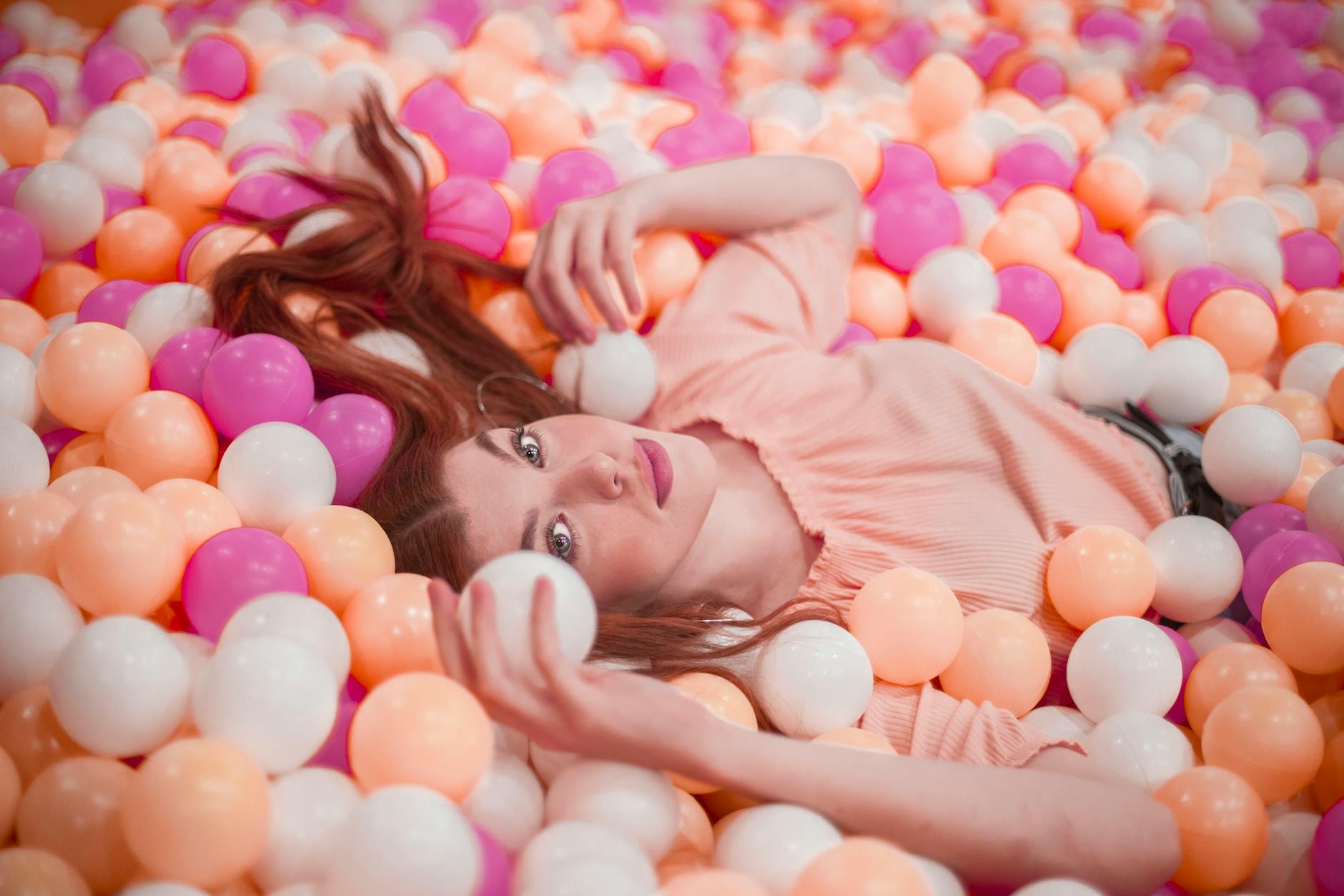 A woman lying in a vibrant ball pit filled with colorful balls at an interactive experience