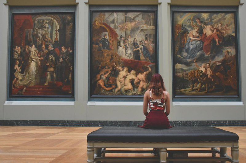 A woman standing in an elegant museum gallery observing classic paintings on the wall