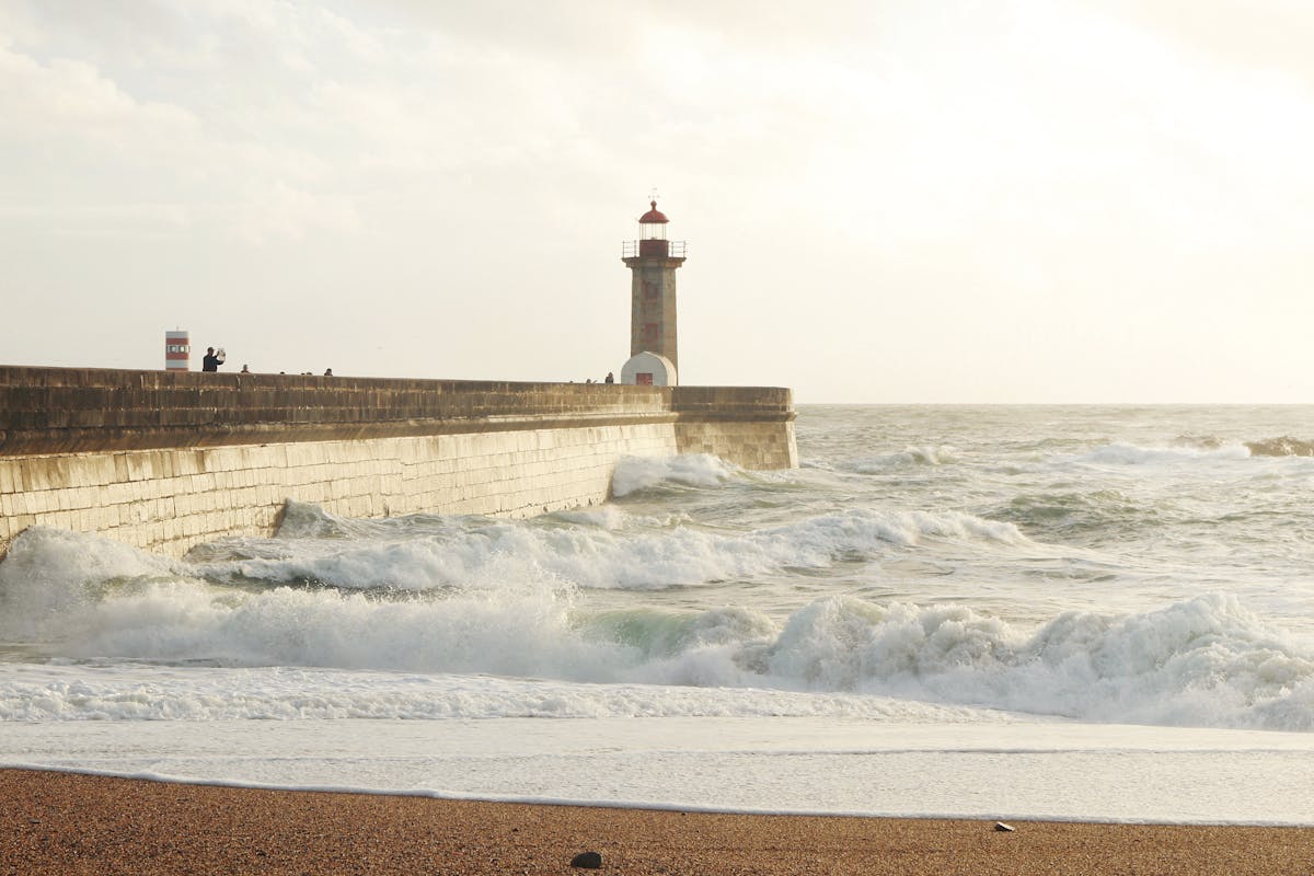 Lighthouse on the breakwater at the mouth of the Douro River with waves crashing during sunset