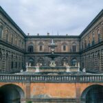 The Renaissance facade of Palazzo Pitti with an ornate stone fountain in the foreground courtyard