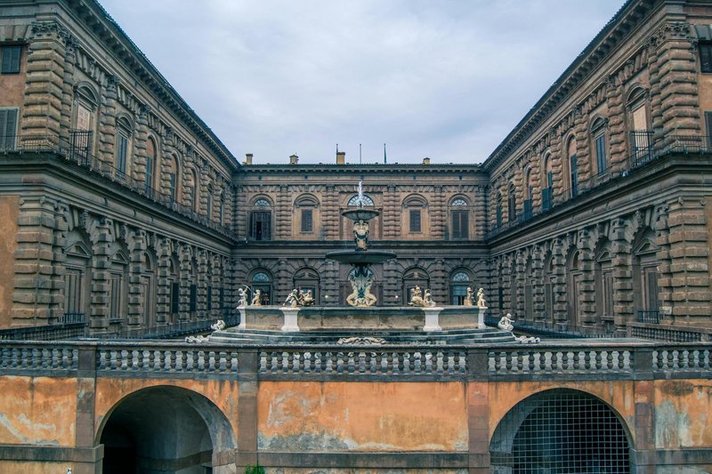 The Renaissance facade of Palazzo Pitti with an ornate stone fountain in the foreground courtyard