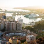 Aerial view of Malaga city with the historic bullring, harbor, and Mediterranean Sea at sunset