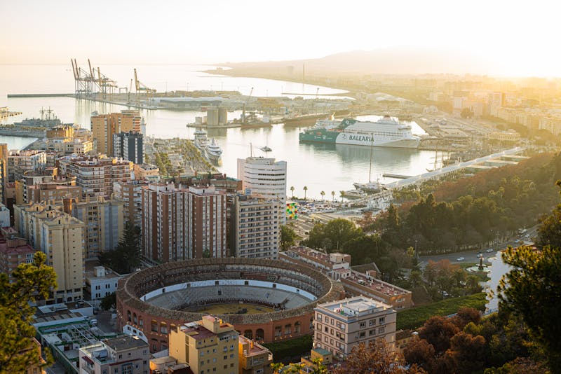Aerial view of Malaga city with the historic bullring, harbor, and Mediterranean Sea at sunset