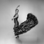 A flamenco dancer mid-performance with arms raised and dress flowing