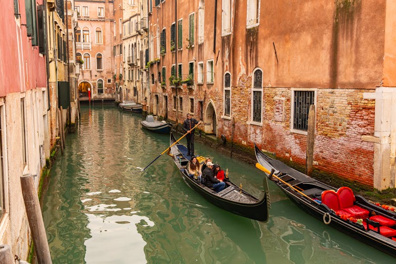 Black gondolas moored along a narrow Venetian canal flanked by colorful historic buildings