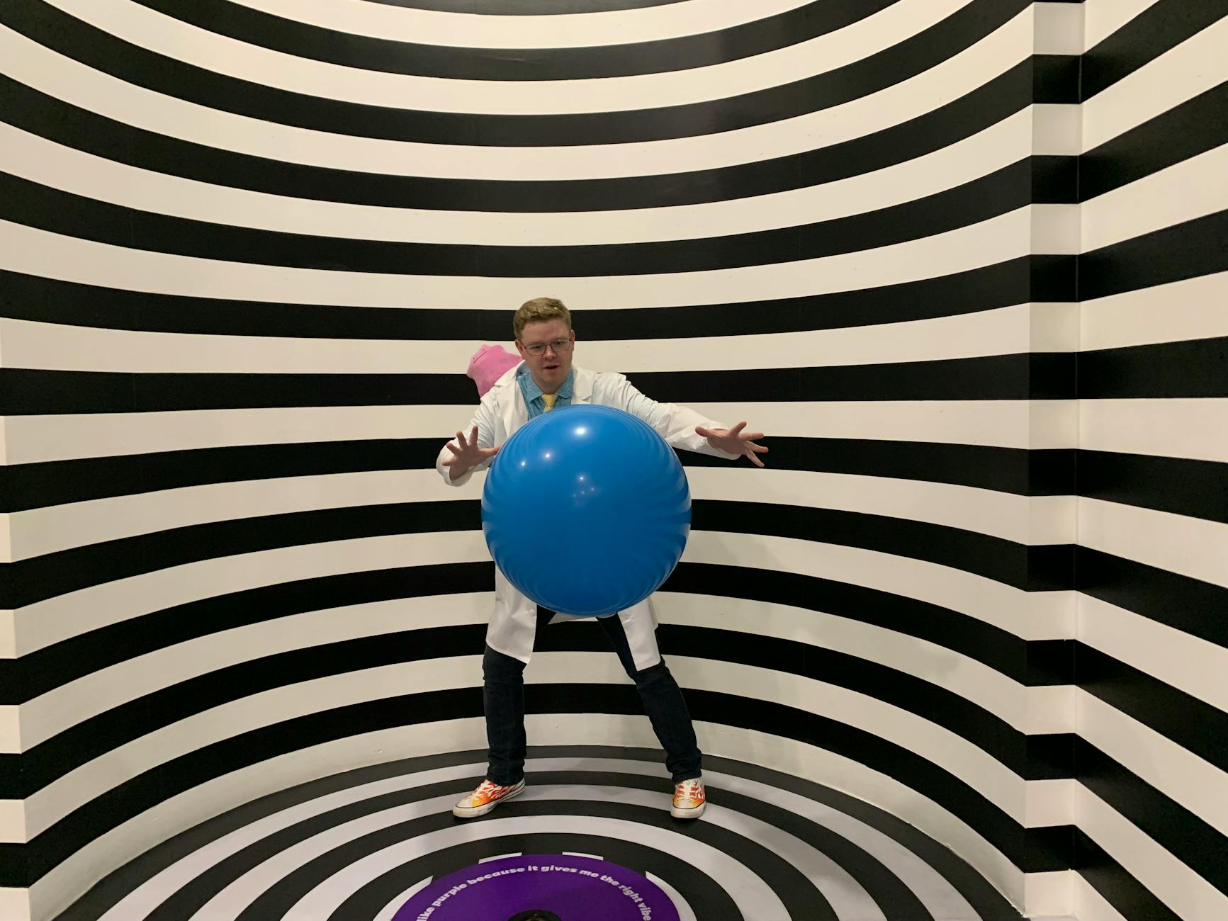 A man posing with a ball in a striped black and white illusion room at an interactive museum