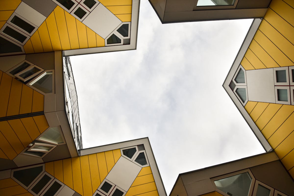 Looking up at yellow cube-shaped buildings with geometric design against a cloudy sky in Rotterdam