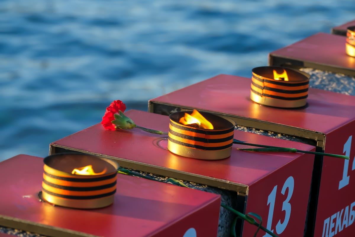 A flame-lit memorial with a red carnation by the water