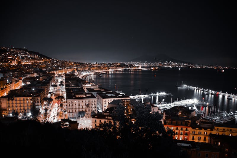 Nighttime aerial view of Naples coastline featuring city lights and serene water