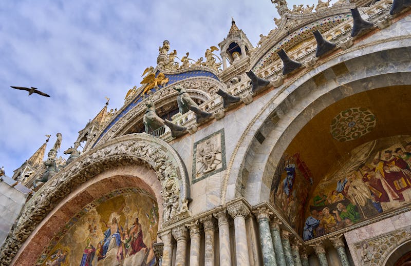 Close-up of carved stonework and golden mosaic panels on the upper facade of St Marks Basilica