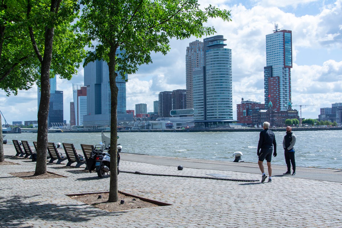 People enjoying a walk by the river with Rotterdam city skyline in the background