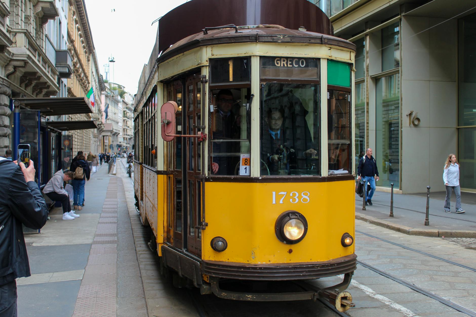 A historic yellow tram passing through a busy Milan street