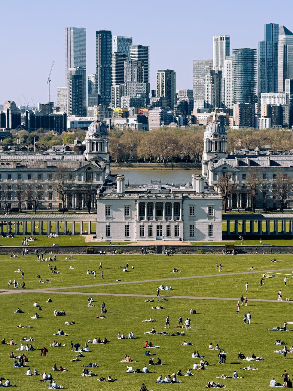 People relaxing in Greenwich Park on a sunny day with the London skyline visible in the background