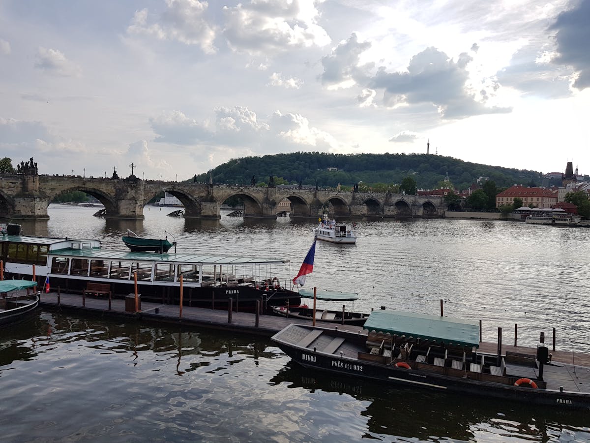 Charles Bridge with boats on the Vltava River in Prague under a cloudy sky